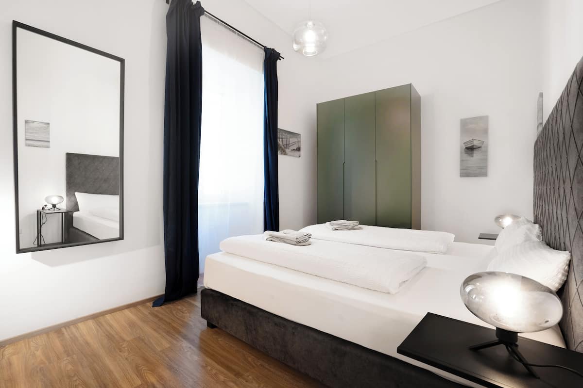Quarto moderno com uma cama grande, mesa de cabeceira com abajur, espelho e obras de arte nas paredes.