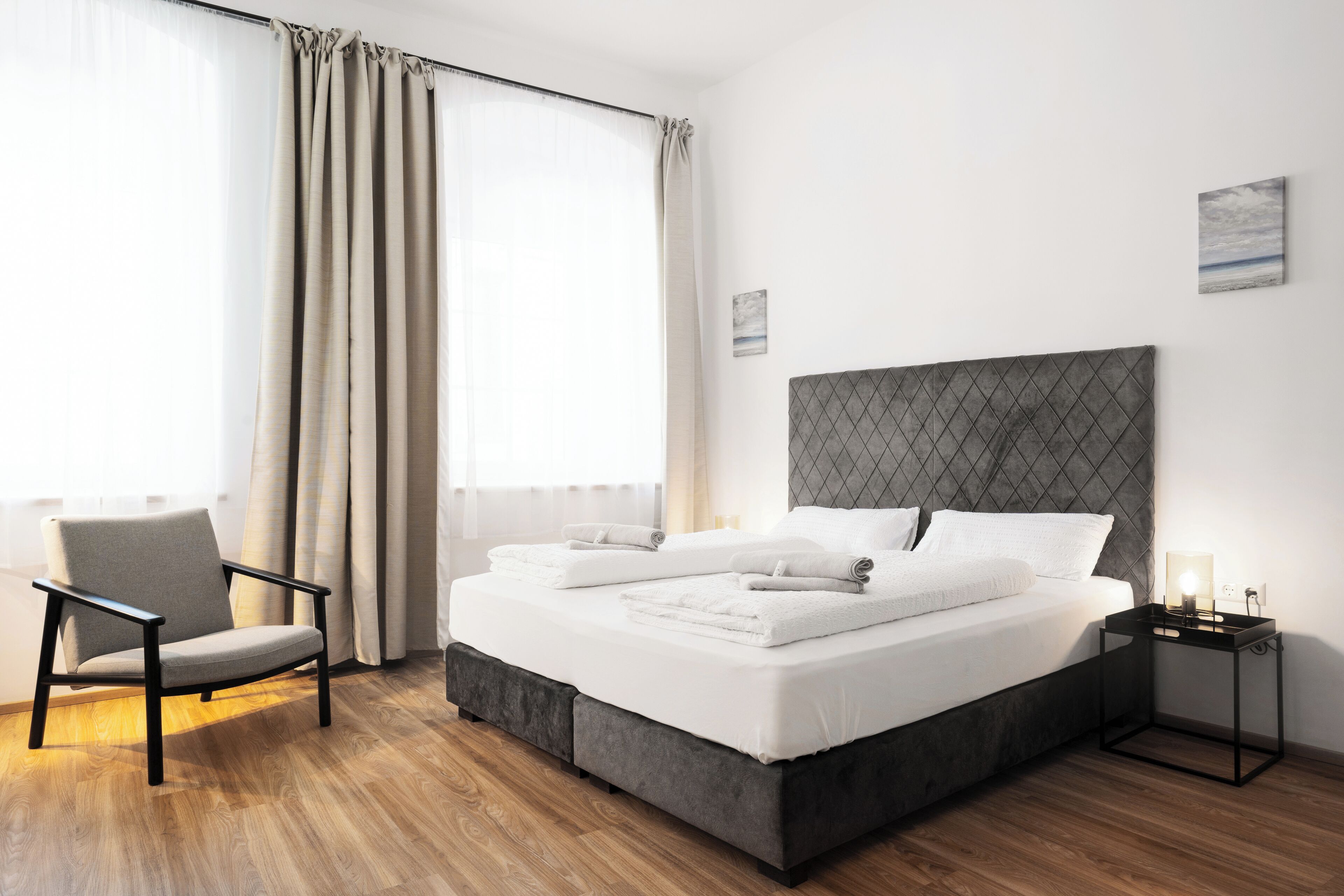 Quarto de hotel moderno com uma cama grande, uma cadeira e uma mesa de cabeceira.