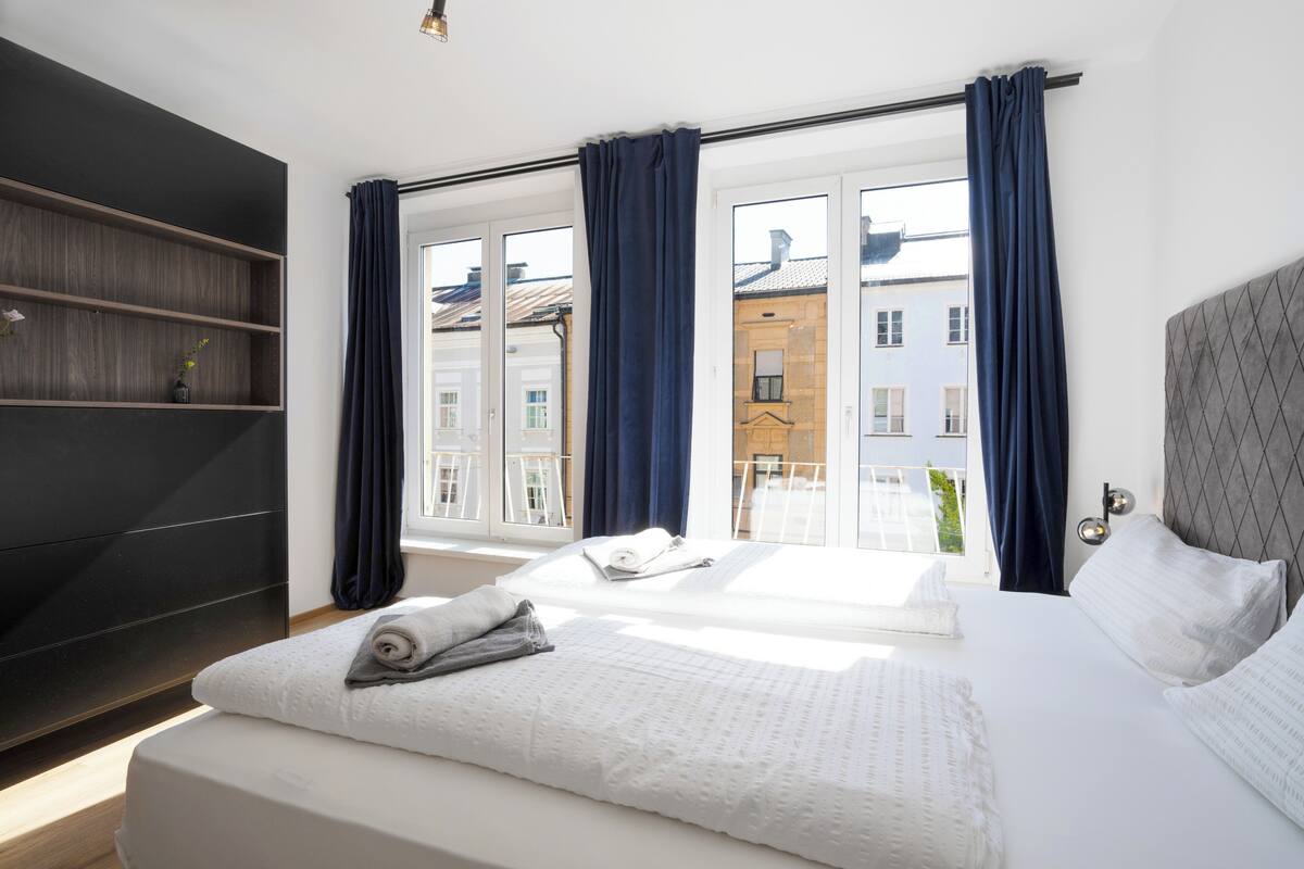 Quarto de hotel com uma cama grande, um guarda-roupa e uma janela com cortinas.