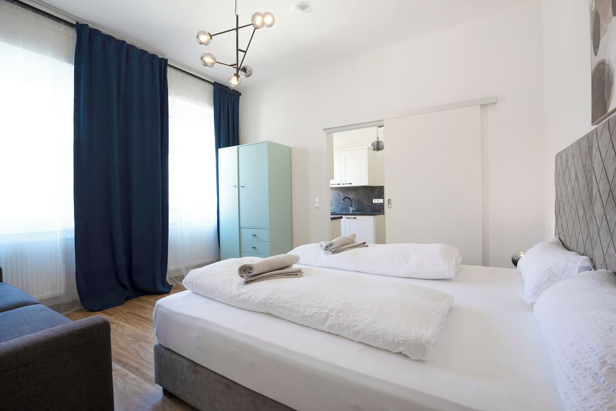 Quarto de hotel moderno com uma cama grande, guarda-roupa, banheiro com espelho e área de refeições.