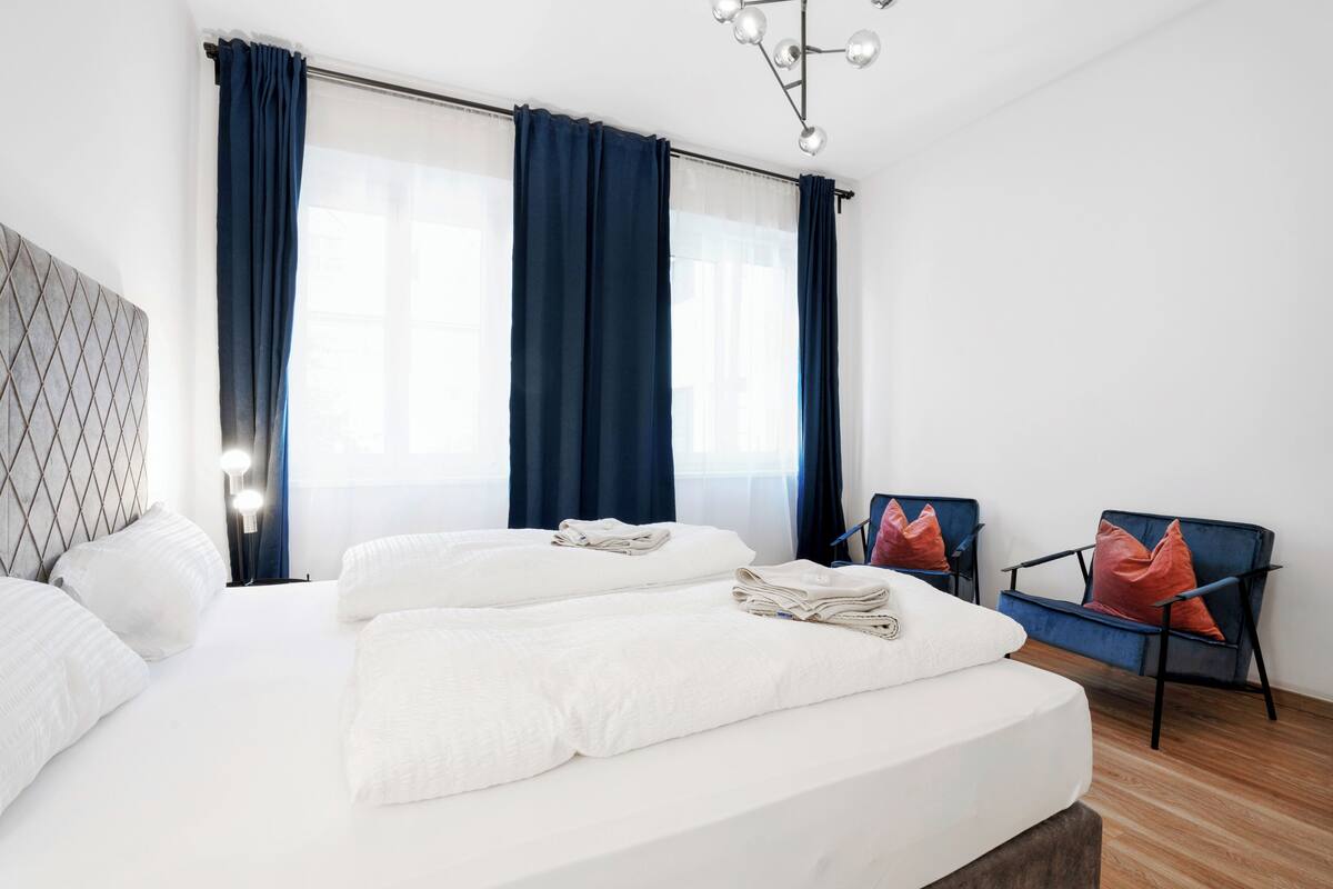 Quarto de hotel moderno com uma cama grande, duas cadeiras e um candelabro.