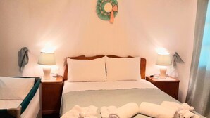 Quarto de hotel com cama, duas luminárias de cabeceira, mesa de apoio, cadeira e porta-toalhas.