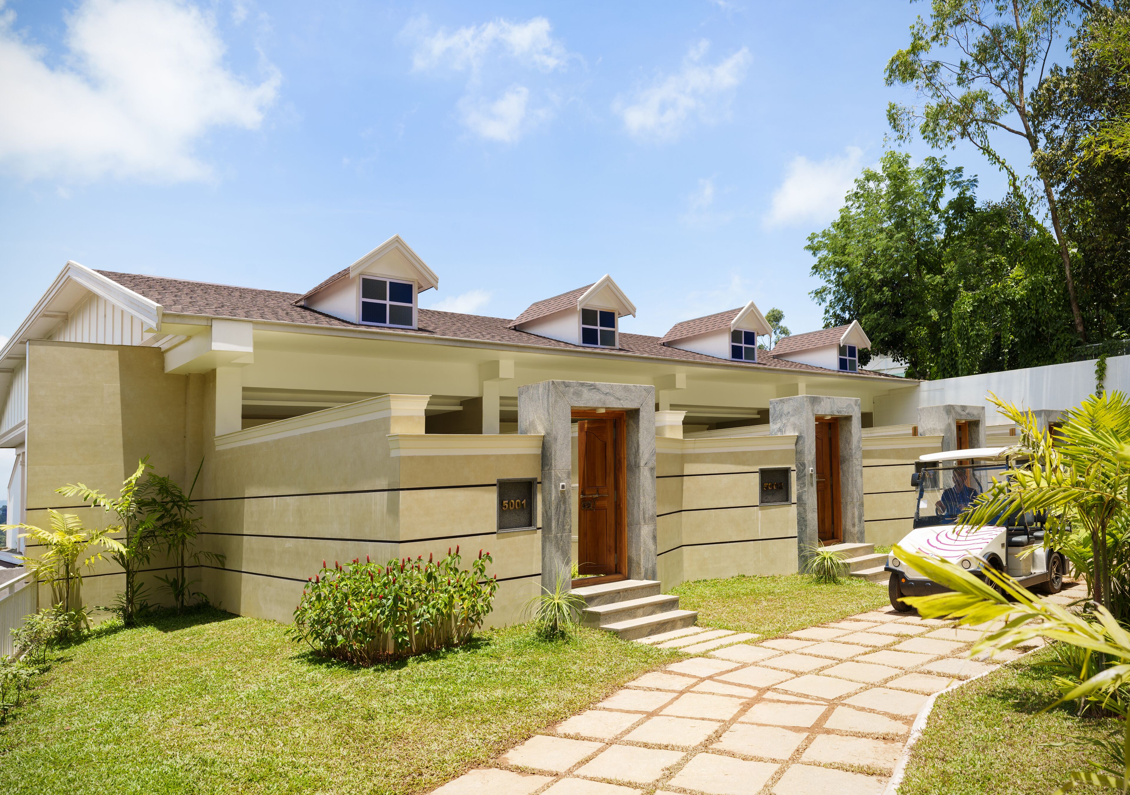 Um edifício moderno com fachada bege, entrada central com porta de madeira e um caminho pavimentado que leva a um carrinho de golfe.