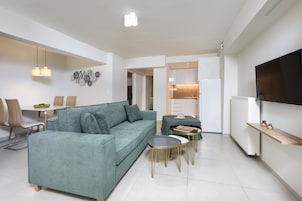 Uma sala de estar moderna com um sofá verde, uma mesa de jantar com cadeiras e uma área de cozinha ao fundo.
