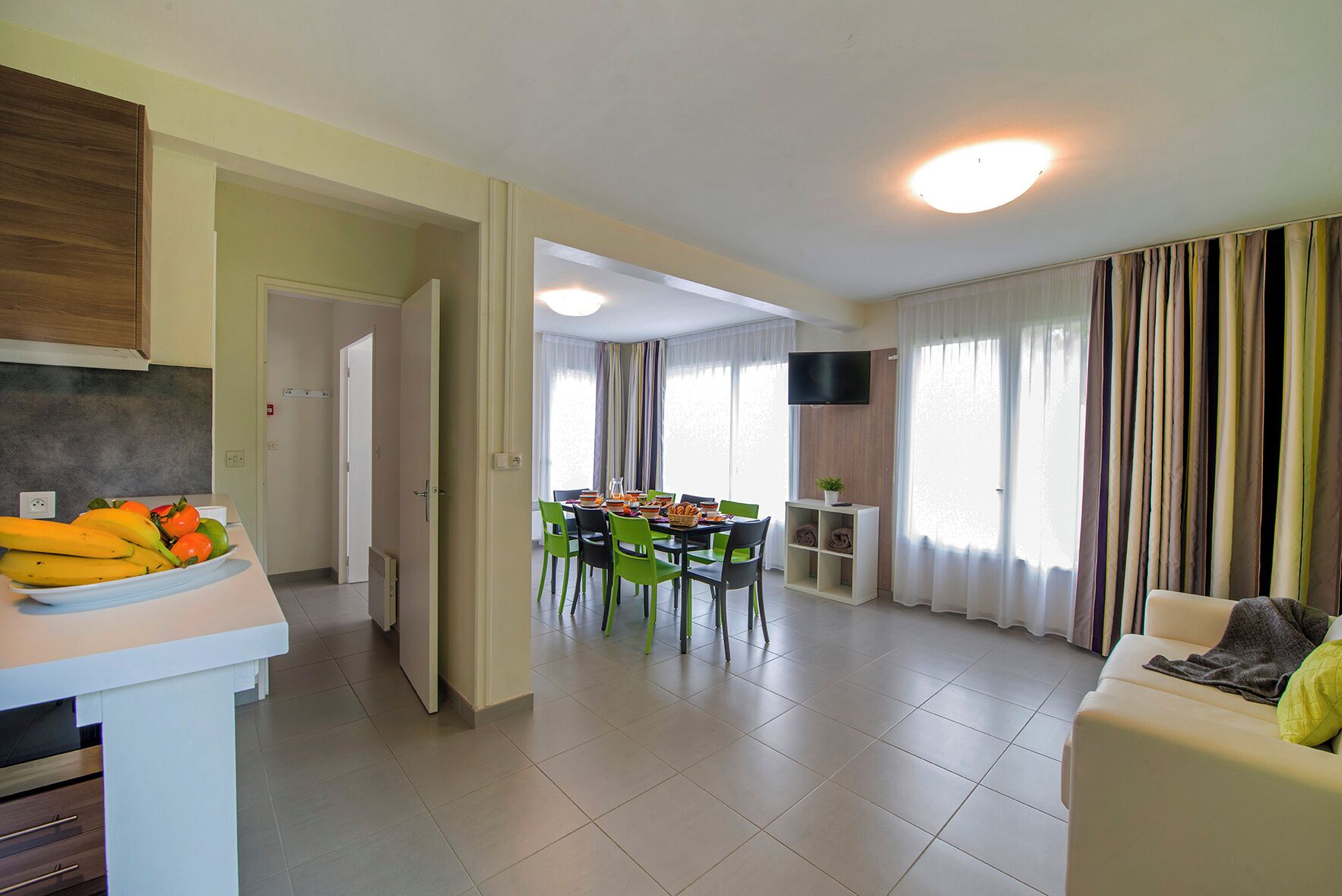 Uma sala de estar moderna com área de jantar, cozinha e televisão na parede.