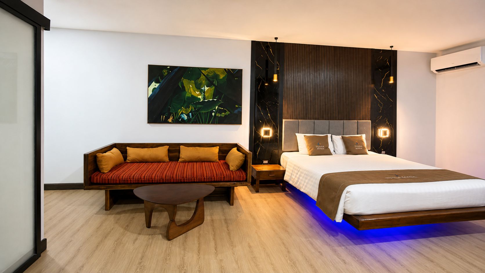 Quarto de hotel com uma cama, um sofá, uma mesinha e um quadro na parede.