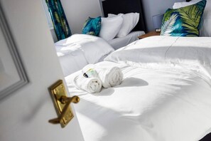 Quarto de hotel com cama bem arrumada, roupa de cama branca e duas toalhas enroladas sobre a cama.
