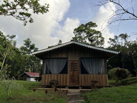 Uma cabana de madeira com telhado pontiagudo, janelas grandes com cortinas e uma porta da frente com painel decorativo.
