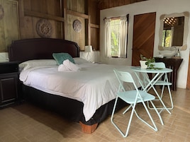 Quarto com cama, mesa de cabeceira, mesa com cadeiras, pia e pratos decorativos na parede.