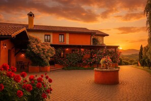 Uma casa com telhado de cerâmica, chaminé e jardim com flores vermelhas.