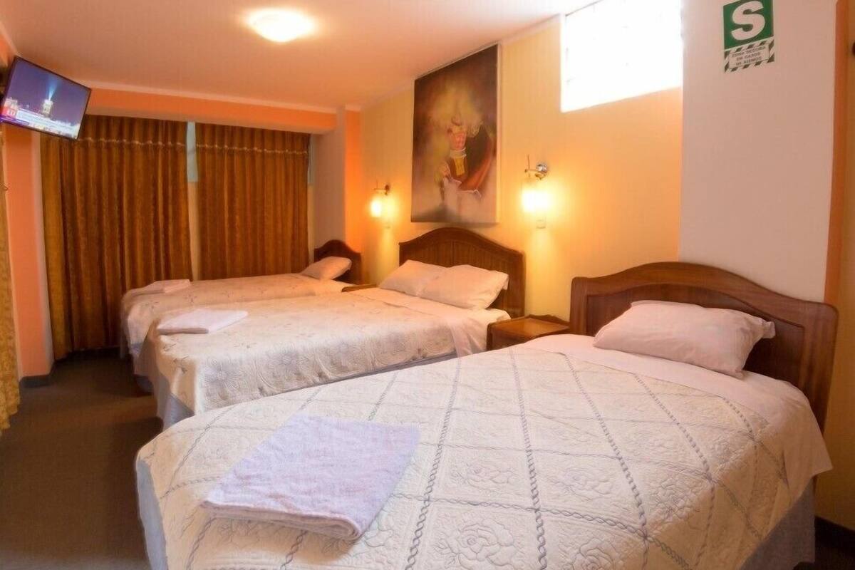 Quarto de hotel com duas camas, uma televisão à esquerda e um quadro na parede.