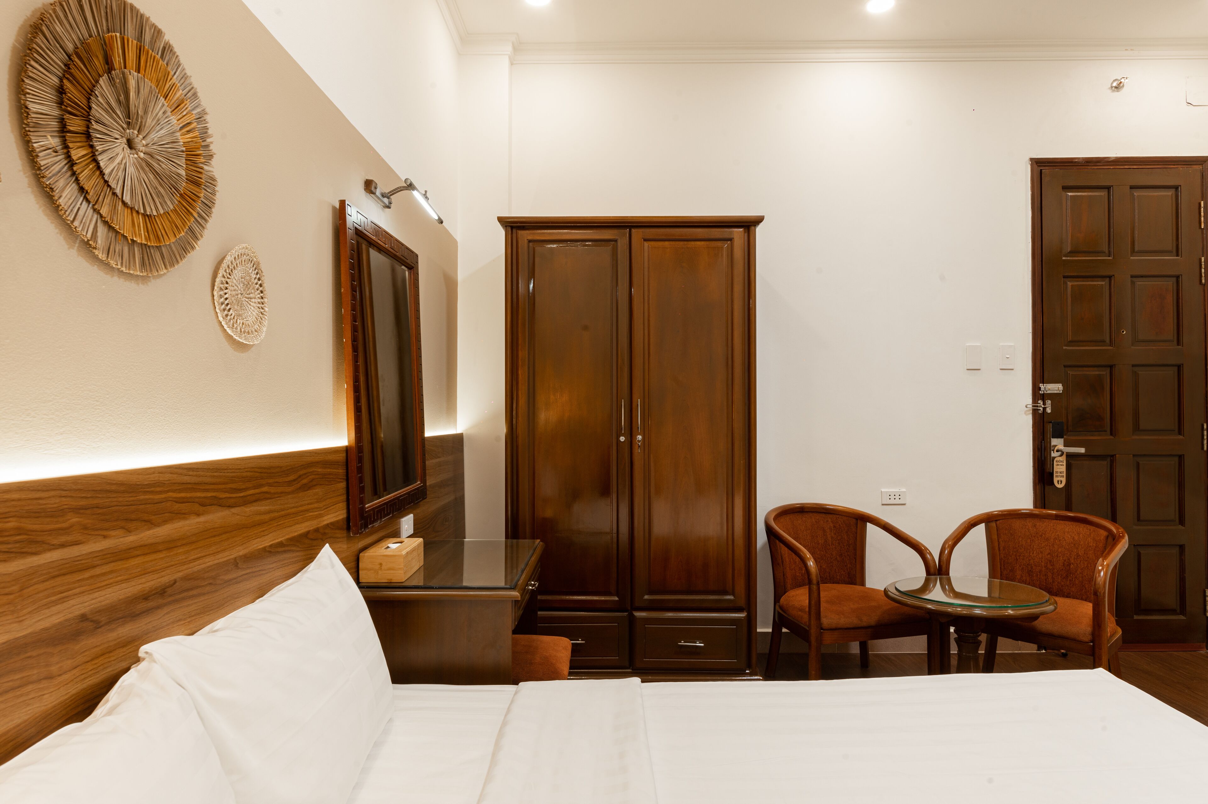 Quarto de hotel com uma cama, uma escrivaninha com espelho, duas cadeiras, um guarda-roupa e uma mesa redonda.