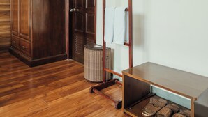 Quarto com piso de madeira, um guarda-roupa, uma porta, porta-toalhas e uma pequena mesa com cestos.