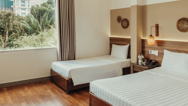 Quarto de hotel com duas camas de solteiro, uma cama grande, uma mesa redonda com bebidas e uma janela com vista para áreas verdes e edifícios.