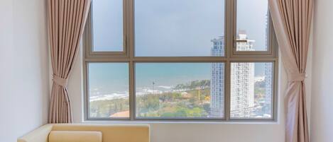 Quarto com uma janela grande, cortinas bege e um sofá bege.
