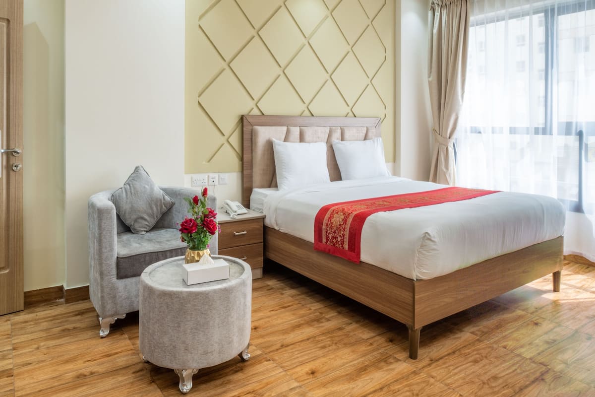 Quarto de hotel moderno com cama de madeira, sofá cinzento, mesa lateral redonda e painel decorativo na parede.