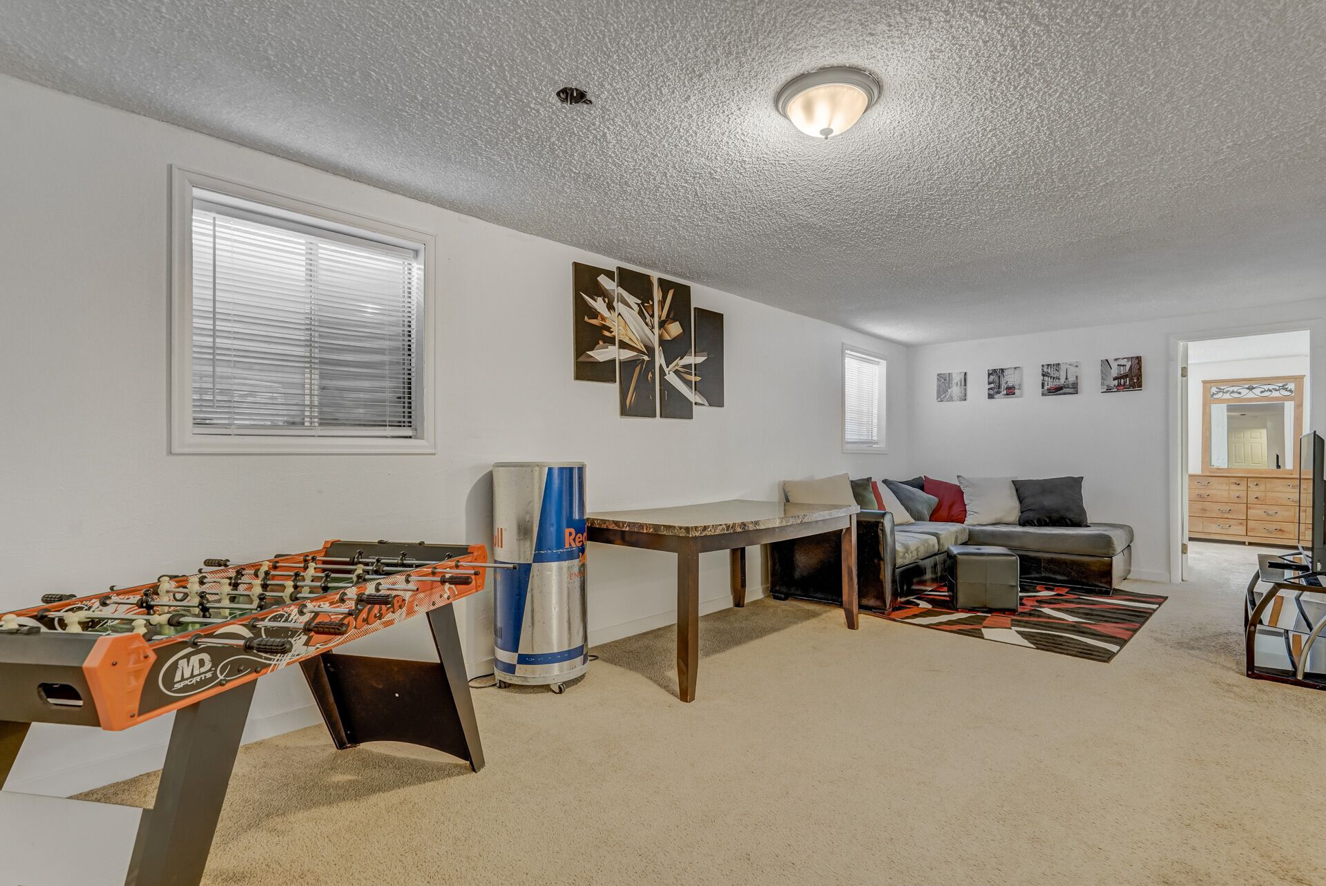Sala de estar com mesa de pebolim, sofá, mesa de centro e rack para TV.