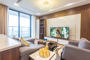 Uma sala de estar moderna com uma grande televisão de tela plana, assentos confortáveis, uma mesa de centro e vista para a cidade através de amplas janelas.