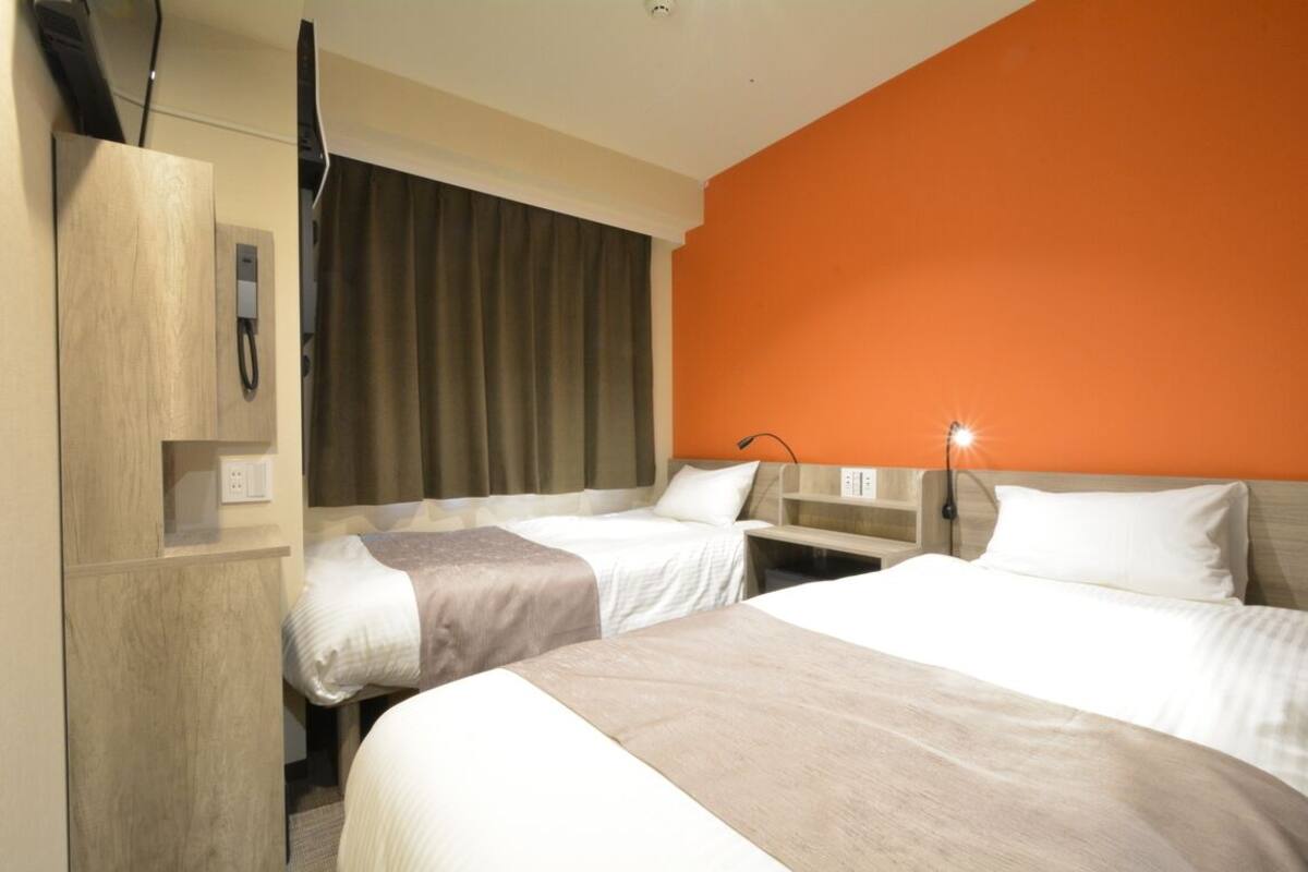 Quarto de hotel com duas camas, uma escrivaninha, uma cadeira, uma televisão e uma tomada.