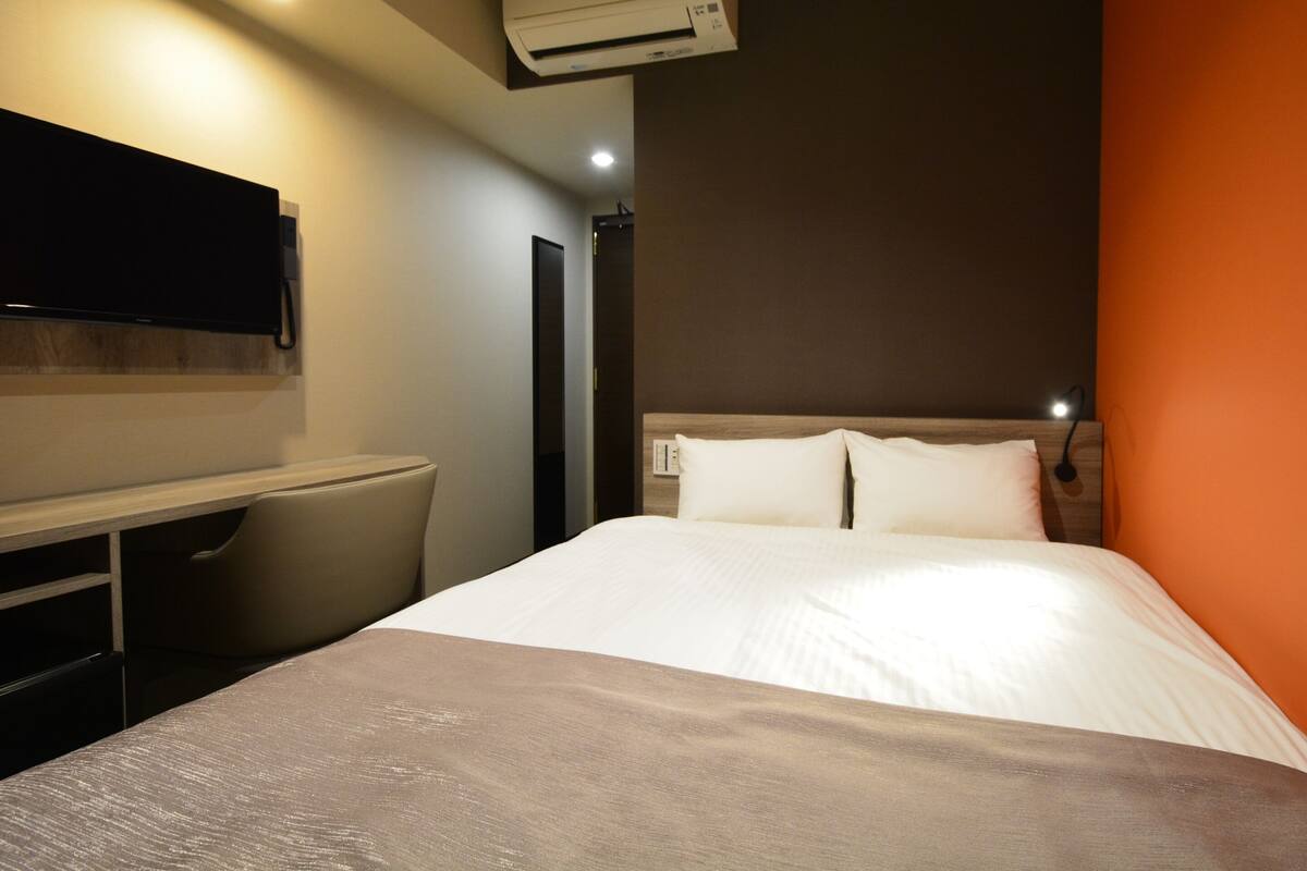 Quarto de hotel com cama, televisão de tela plana na parede, mesa de cabeceira e aparelho de ar condicionado.