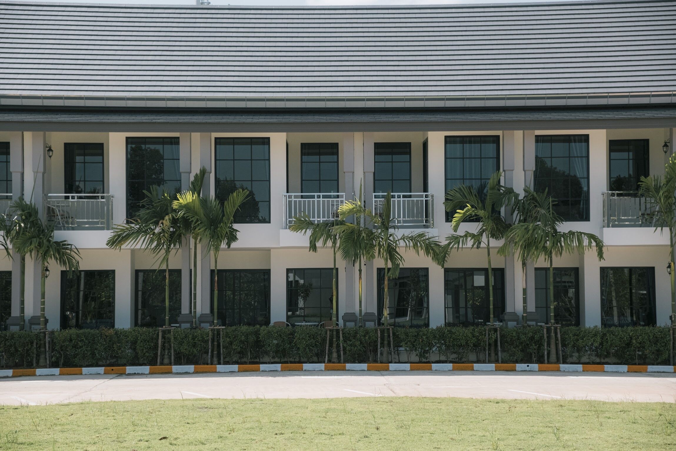 Um edifício moderno com telhado plano, várias janelas e uma varanda com guarda-corpo.