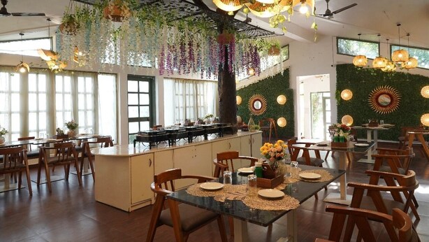 Um restaurante com mesas e cadeiras de madeira, plantas penduradas e arandelas decorativas.