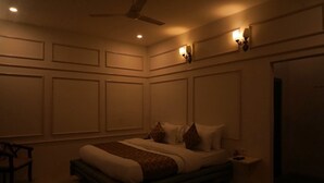 Um quarto com iluminação fraca, uma cama, uma mesa de cabeceira, uma cadeira e um ventilador de teto.