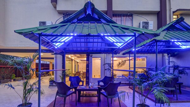 Uma área de estar externa com um gazebo coberto, plantas em vasos e vista para o interior do edifício.