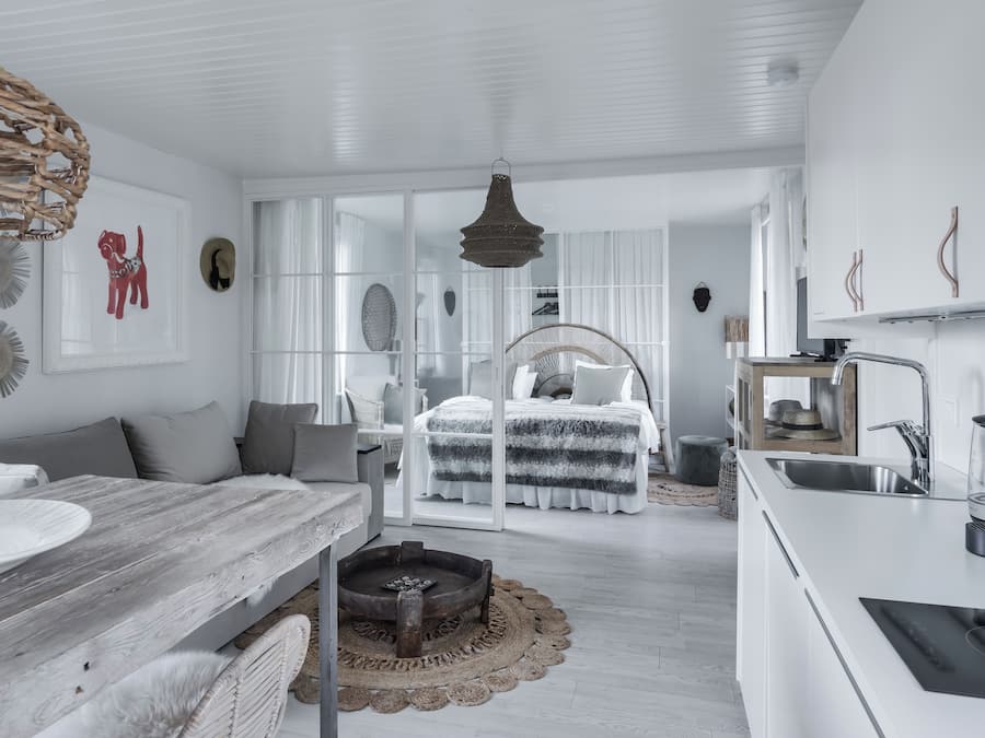 Quarto moderno e minimalista com uma cama grande, um espaço de estar separado e uma cozinha compacta.