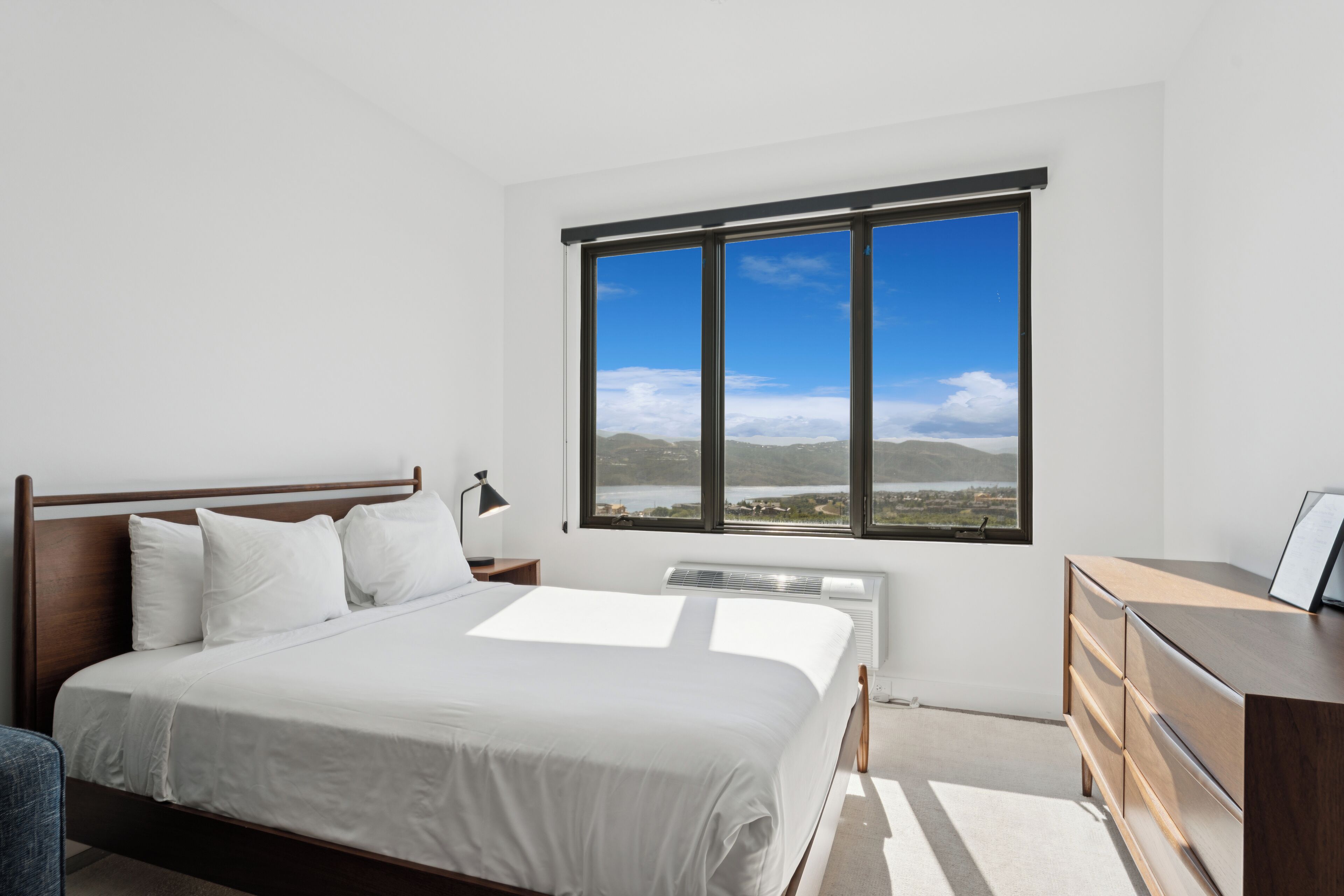 Quarto com uma janela grande, uma cama, um aparador e uma mesinha de cabeceira.