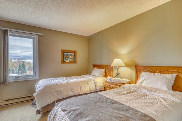 Quarto de hotel com duas camas, janela com cortinas, mesa de cabeceira com abajur e um quadro na parede.