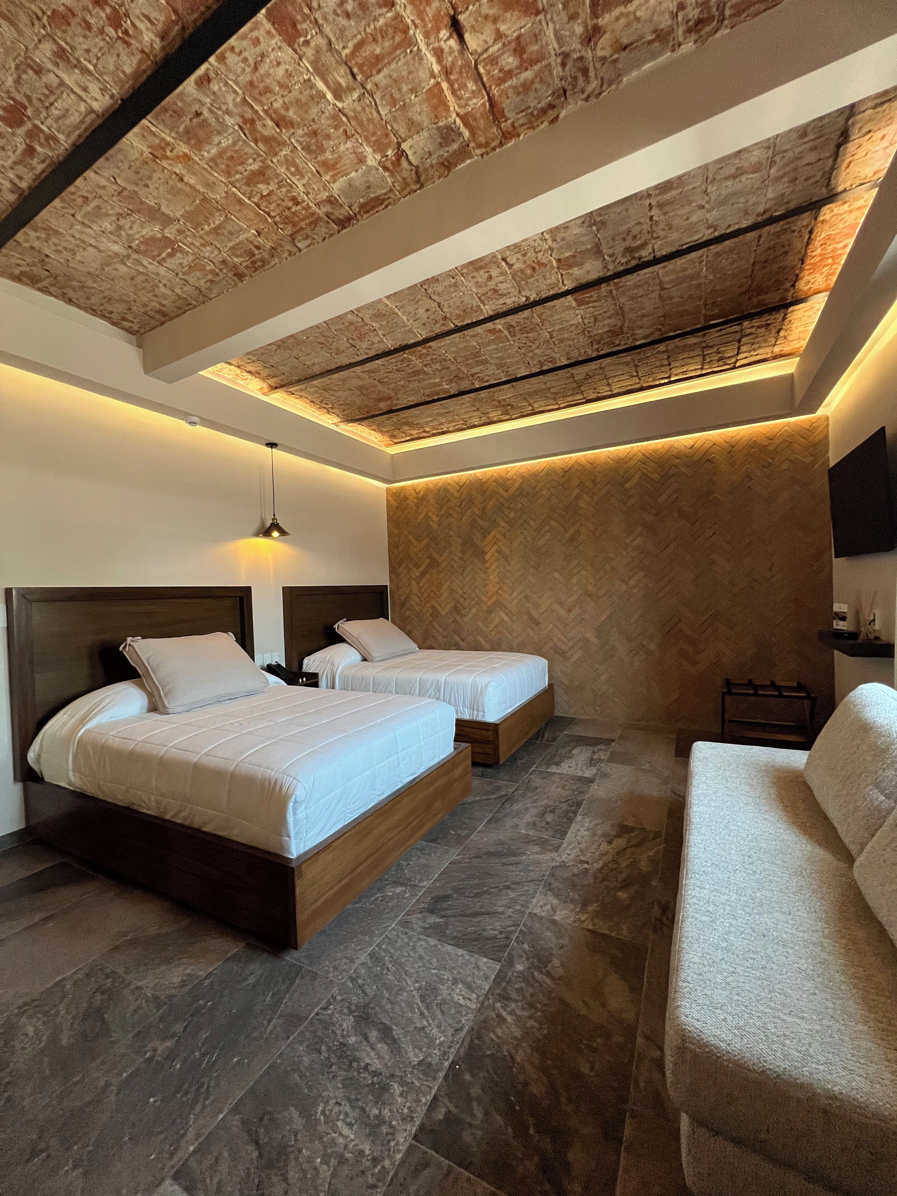 Quarto moderno com duas camas, um sofá e parede com padrão em herringbone.