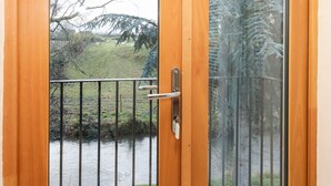 Uma porta de madeira com puxador de metal e vista para um rio e vegetação.