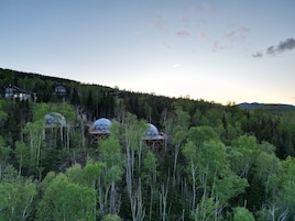 Uma área arborizada com diversas estruturas em formato de cúpula, provavelmente usadas para hospedagem ou observação, cercada por árvores densas e uma montanha ao fundo.