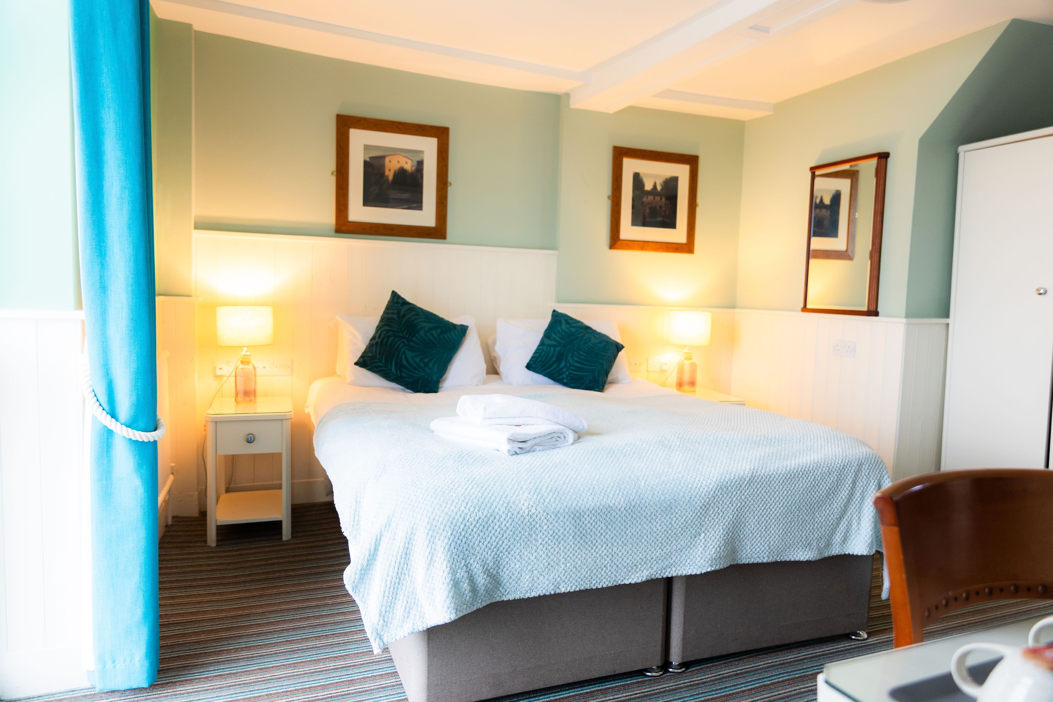 Quarto de hotel com cama, duas mesas de cabeceira com luminárias, uma cadeira e um guarda-roupa.