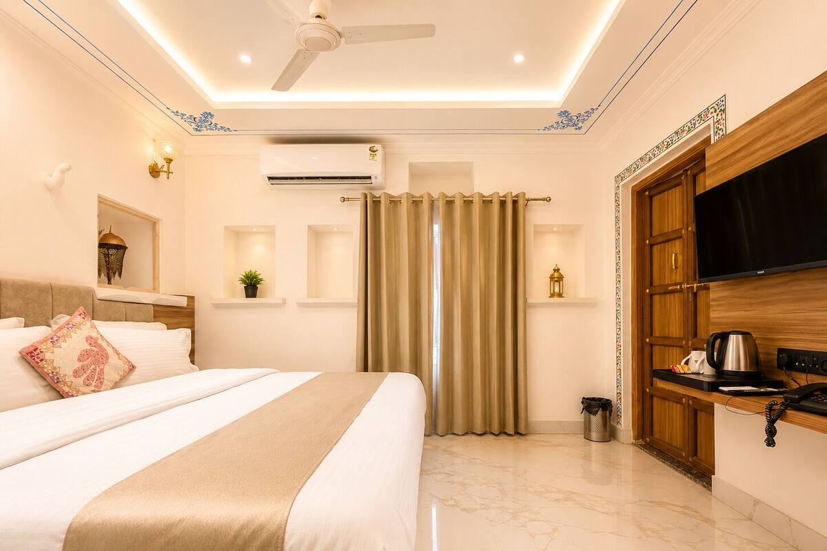 Quarto de hotel com uma cama, ventilador de teto, ar condicionado, televisão, cafeteira e uma pequena lixeira.