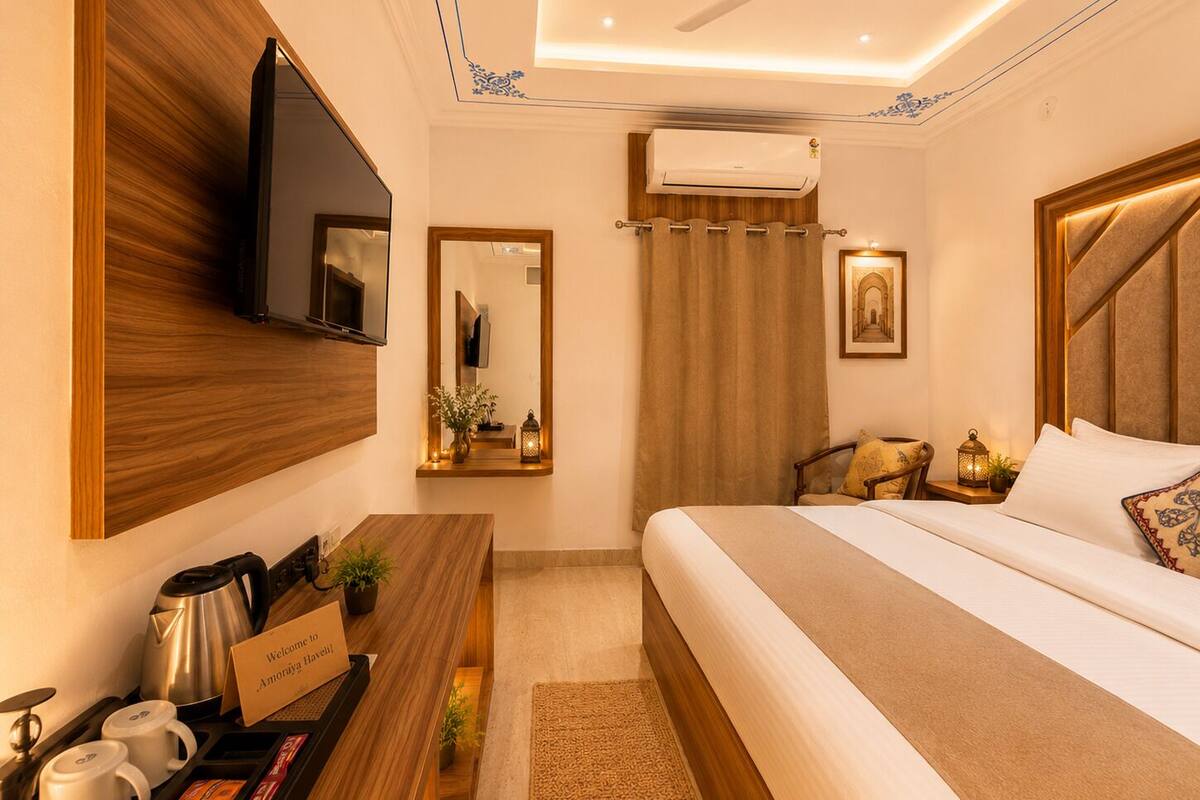 Quarto de hotel com cama, mesa de cabeceira com cafeteira, televisão na parede e aparelho de ar condicionado.