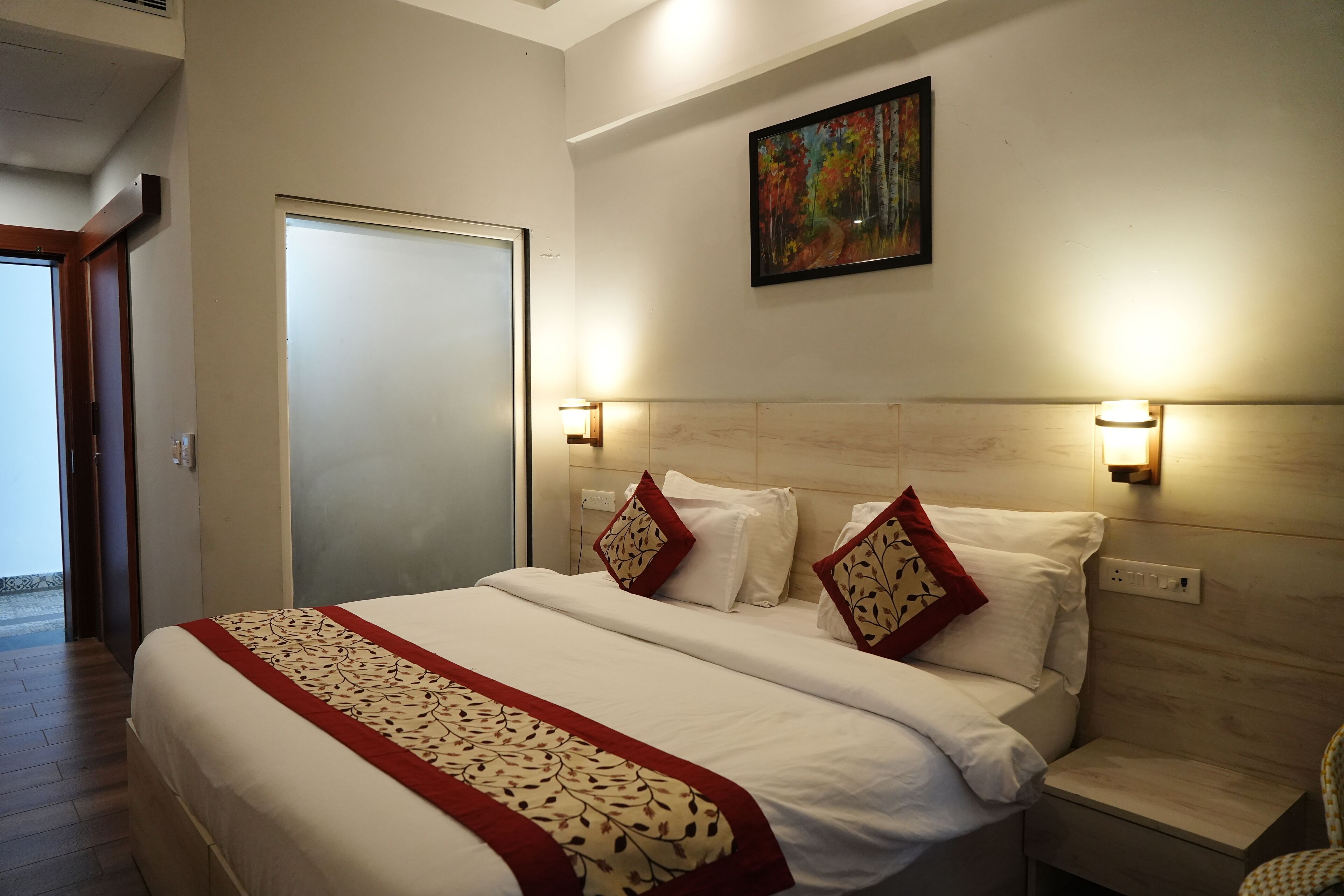 Quarto de hotel com uma cama grande, duas luminárias de cabeceira, um quadro na parede e uma porta que dá para uma varanda.