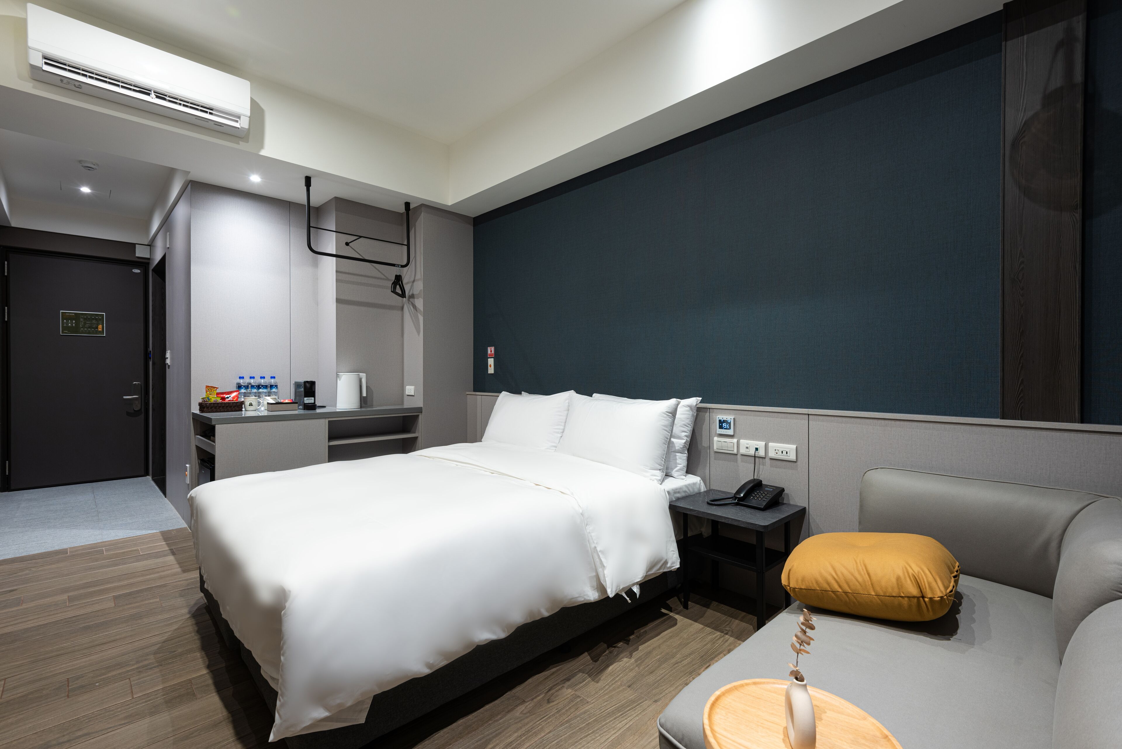 Quarto de hotel moderno com uma cama grande, uma escrivaninha, uma cadeira e uma parede de destaque escura.