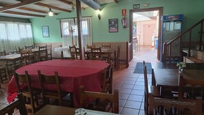 Um restaurante com mesas e cadeiras de madeira, toalha de mesa vermelha e um letreiro com a palavra 'SALIDA' (saída).