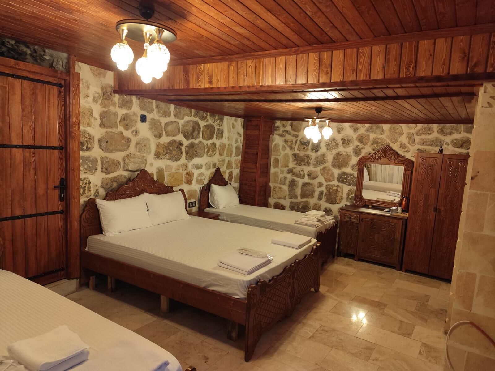 Quarto com parede de pedra, teto de madeira e cama com cabeceira de madeira.
