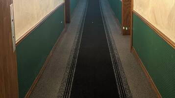 Um corredor de hotel com paredes verdes e bege, carpete preto e uma porta de madeira no final.