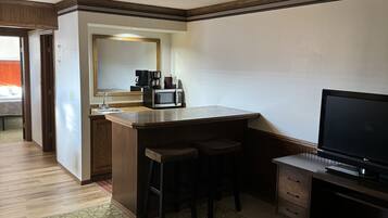 Quarto de hotel com cozinha compacta, um espelho grande, televisão de tela plana e tapete estampado.