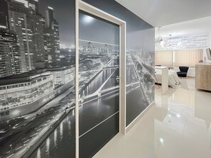Quarto de hotel moderno com um grande mural da paisagem urbana na parede, uma escrivaninha elegante e uma área de estar confortável.