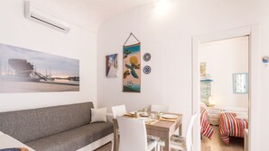 Um espaço compacto com sofá, mesa de jantar, cadeiras e uma pequena cozinha equipada.