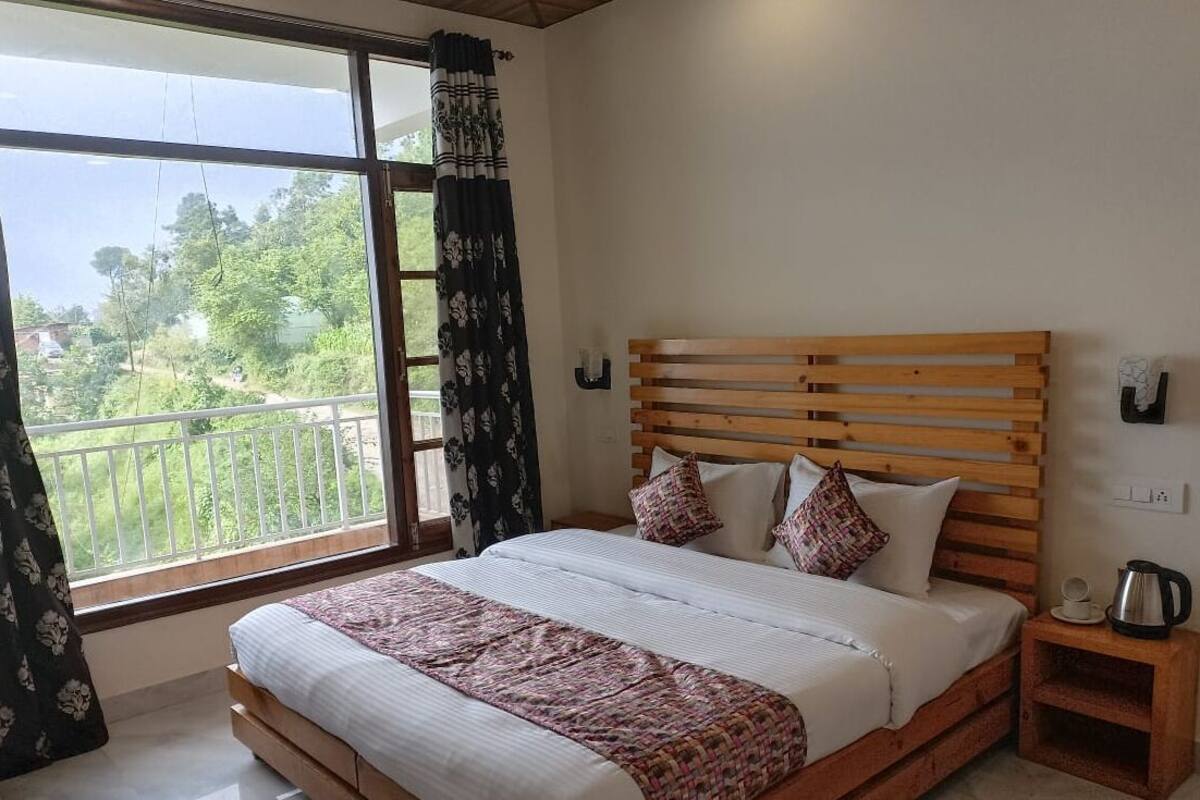Quarto com cama de madeira, roupa de cama branca, vista para o verde lá fora e uma pequena mesa de cabeceira com uma chaleira.