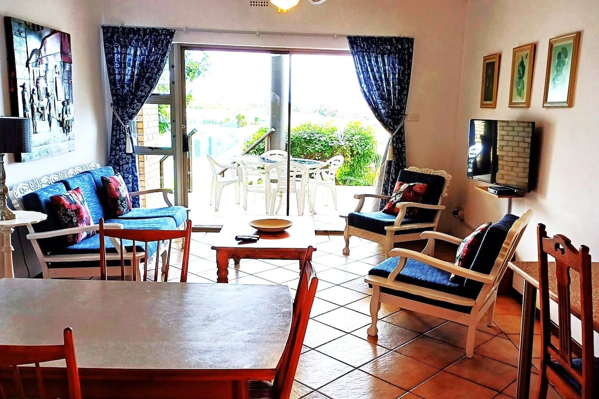 Uma sala de estar com sofá, cadeiras, mesa e televisão.