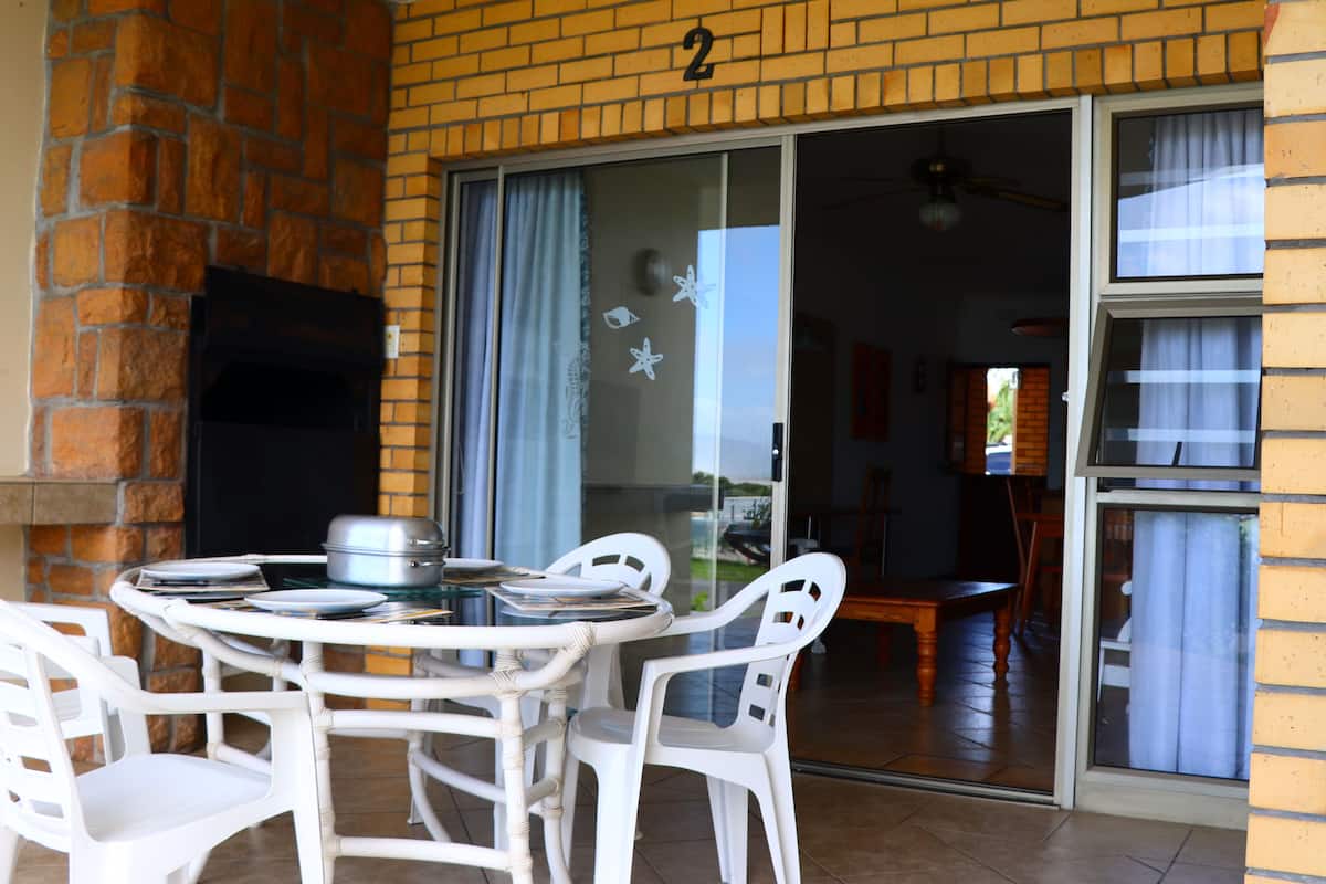 Um pátio com parede de tijolos, porta de vidro que dá para o interior e uma mesa com cadeiras.