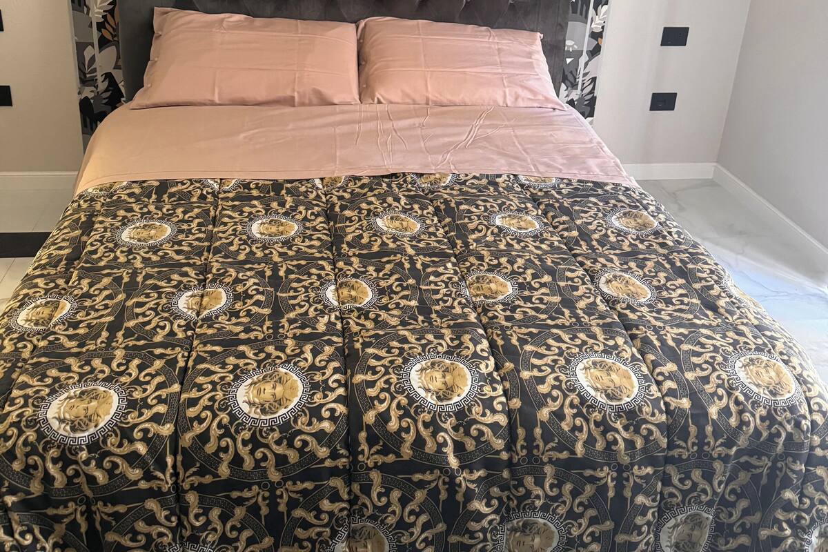 Quarto com cabeceira estofada, colcha estampada e parede com design de folhas e rosto.