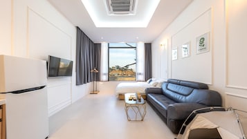 Quarto de hotel moderno com televisão de tela plana, sofá, mesa pequena e cama.